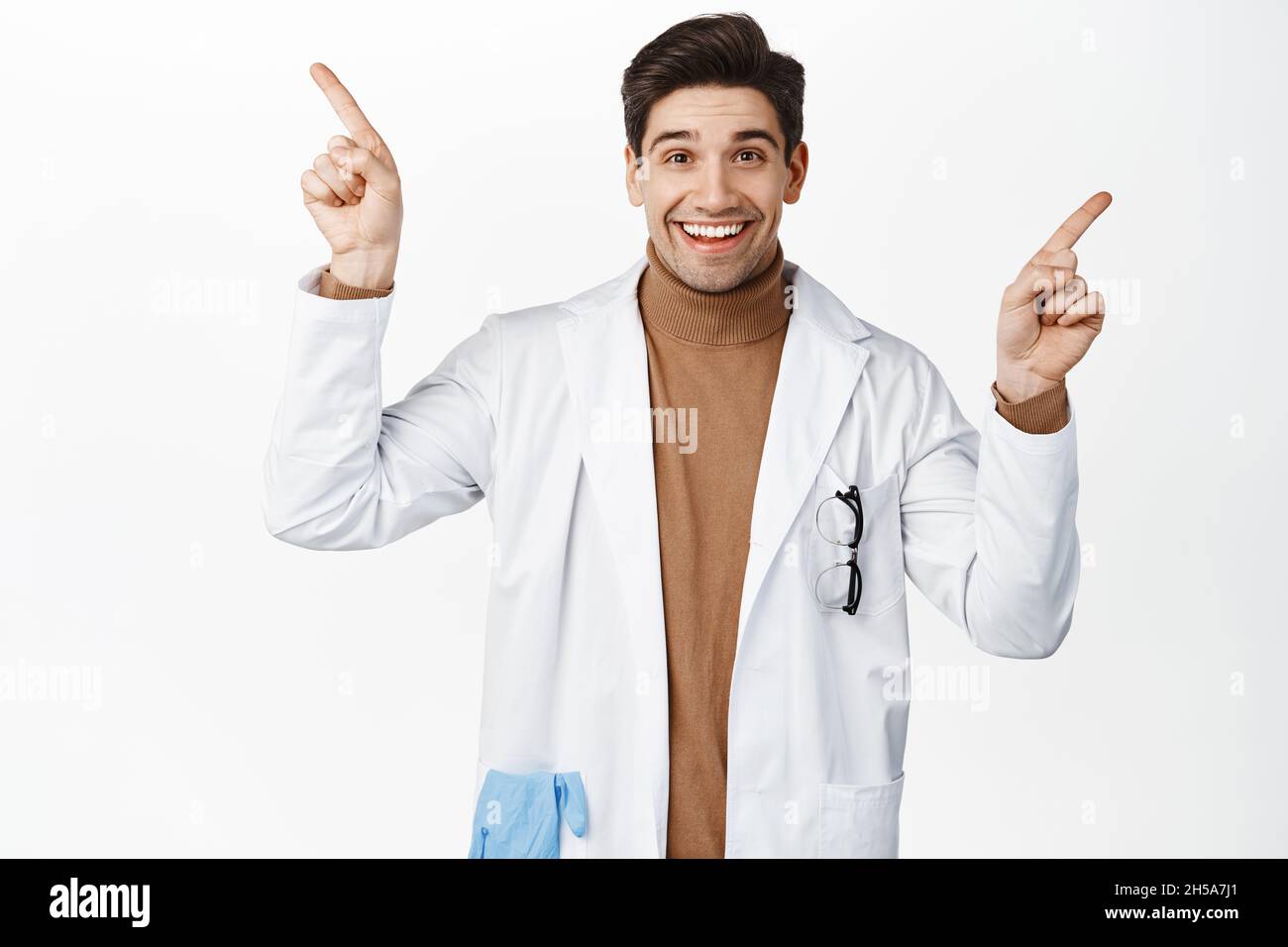 Portrait of smiling handsome doctor pointing fingers sideways, showing ...