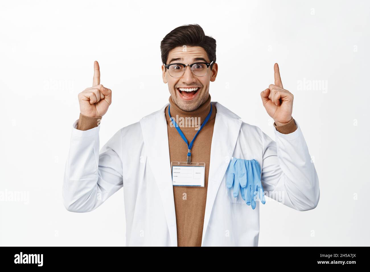 Smiling doctor in medical robe, pointing fingers up, showing ...