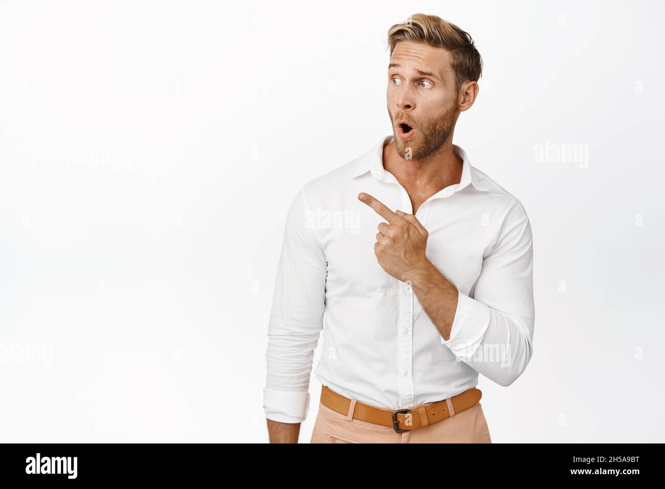 Portrait of handsome blond man pointing and looking left with amazed ...