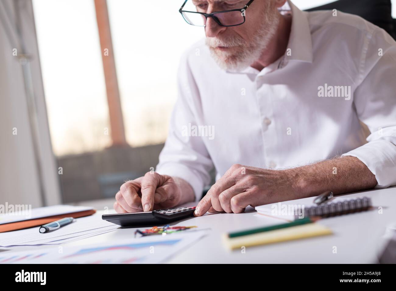 Senior businessman using a calculator in office, hard light Stock Photo ...