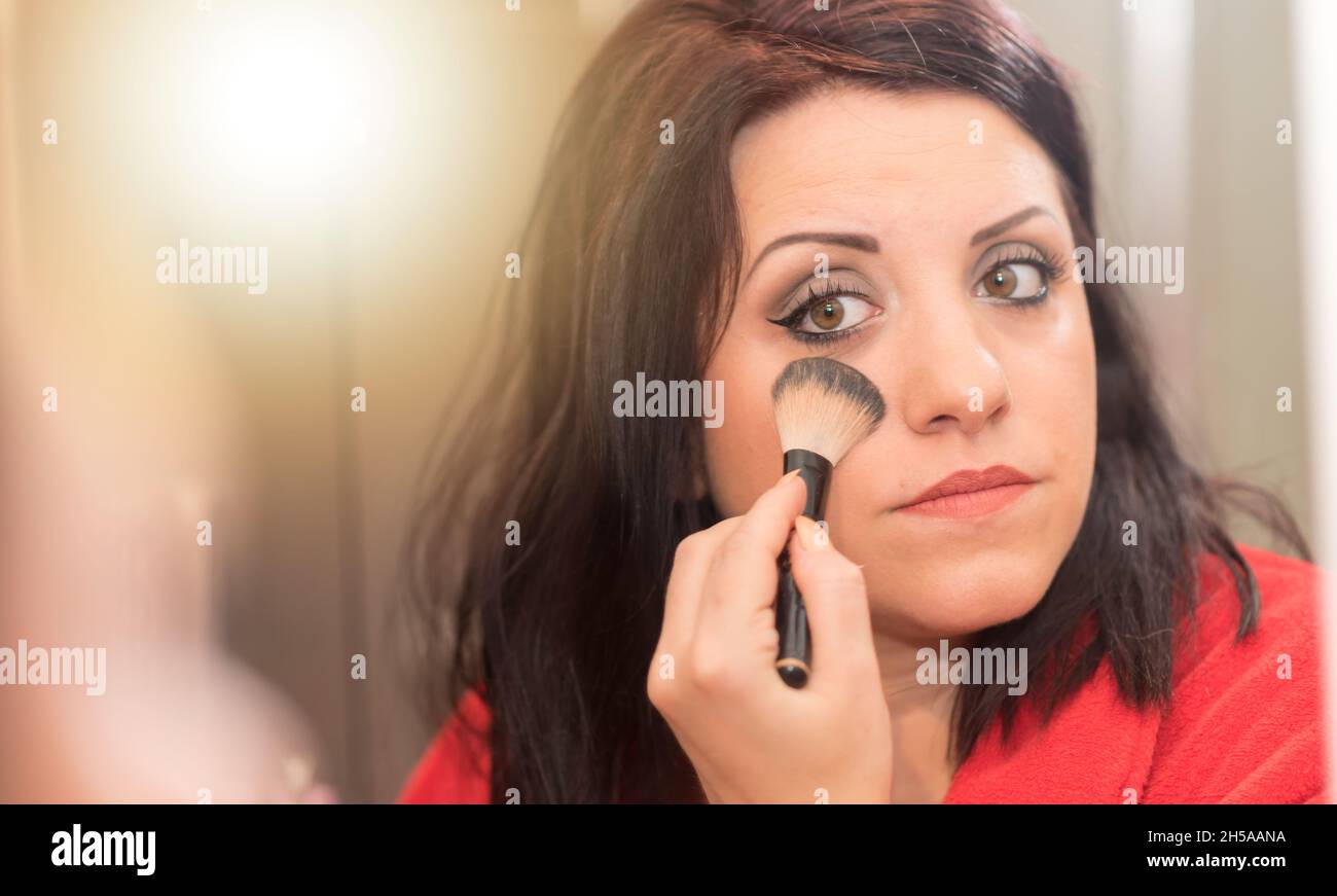 Beautiful brunette applying cosmetic powder on her face, light effect ...