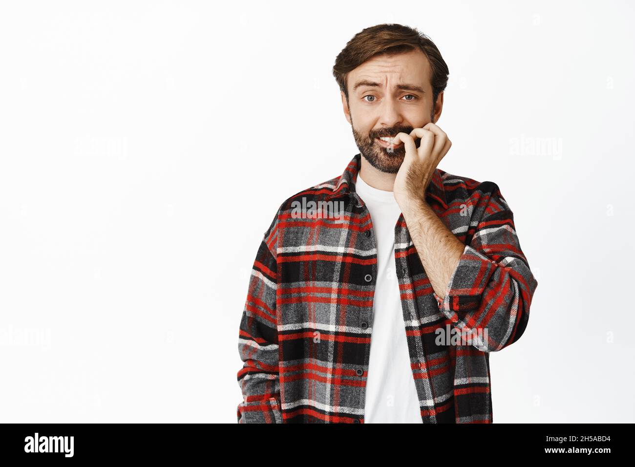 Portrait of scared bearded man biting his finger nails, looking anxious ...