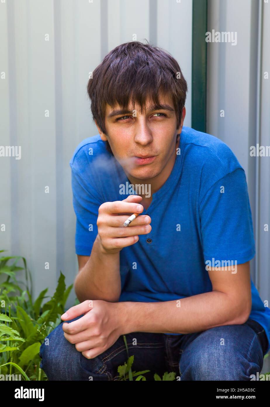 Young Man sitting and smoking Cigarette by the Wall outdoor Stock Photo ...