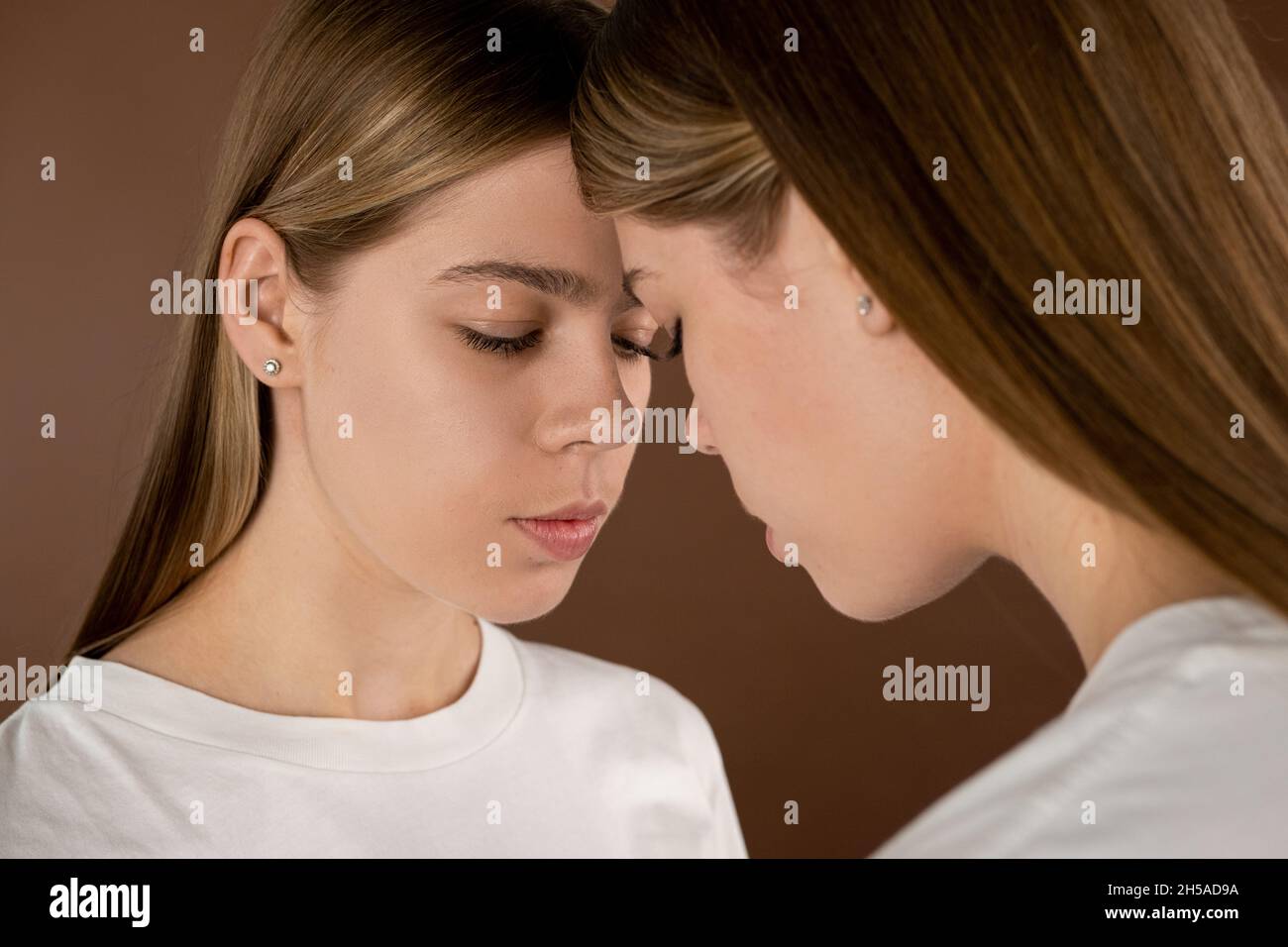 Pretty teenage twin girls touching by foreheads while standing in front ...