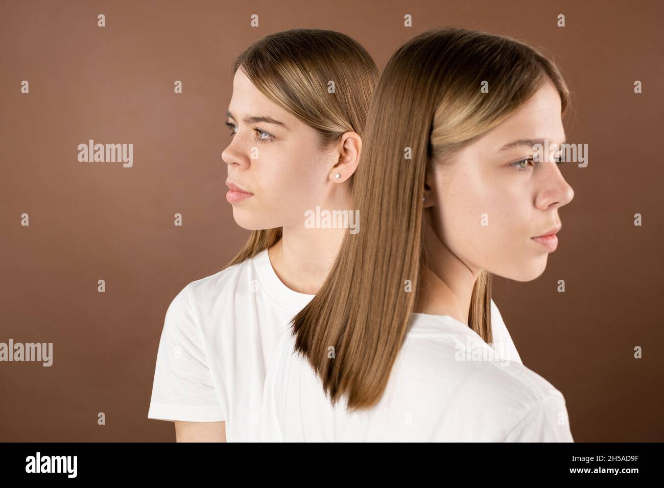 Serene twin girls with long blond hair looking in opposite direction ...