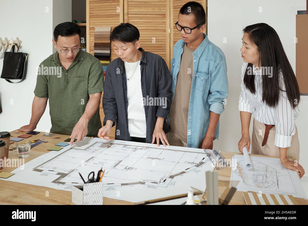 Group of young architects gathered by table with large sketch on ...