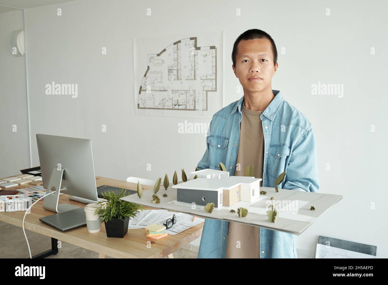 Young confident architect holding house layout while standing in front ...