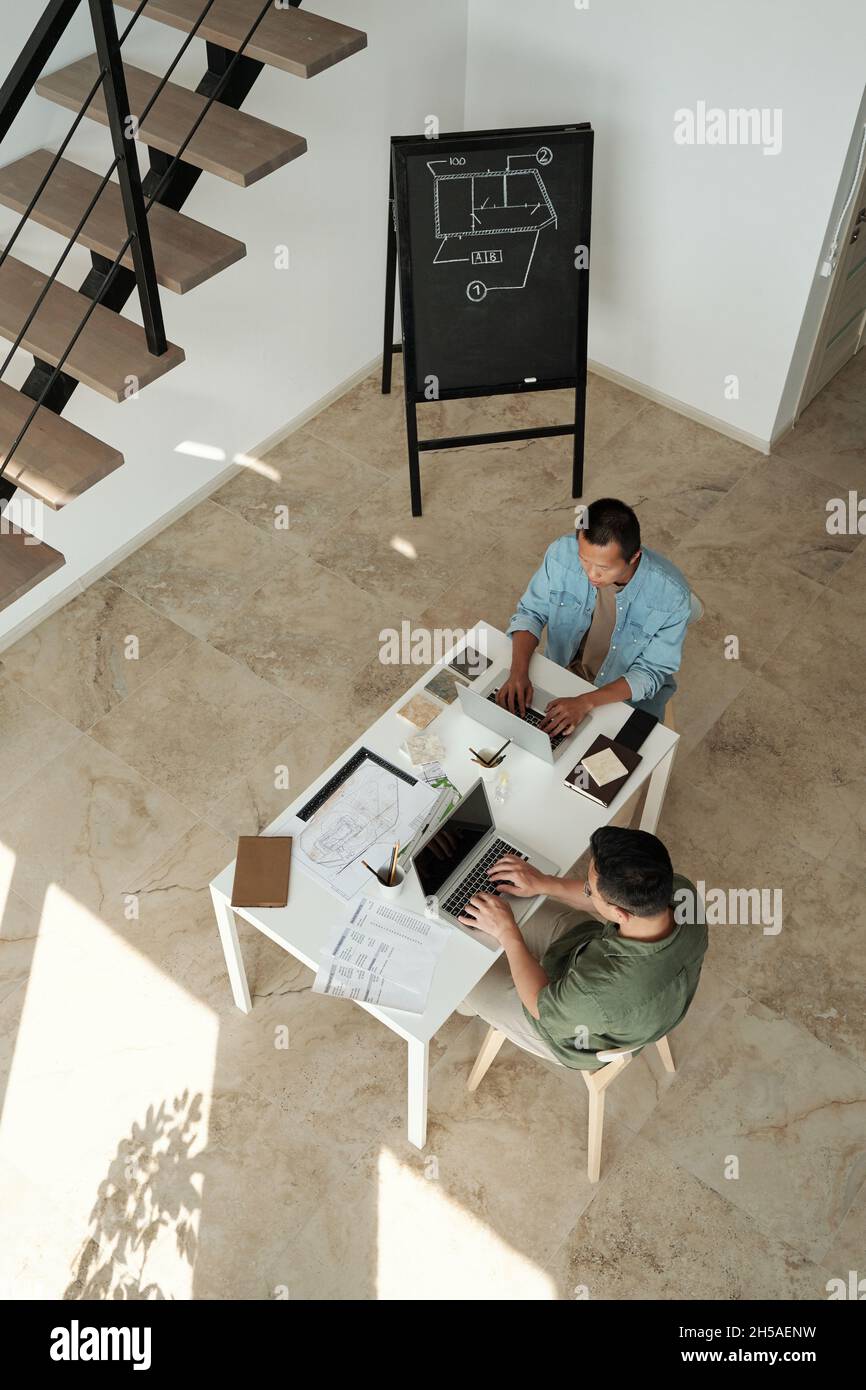 Two young busy office workers sitting in front of laptops by table and ...