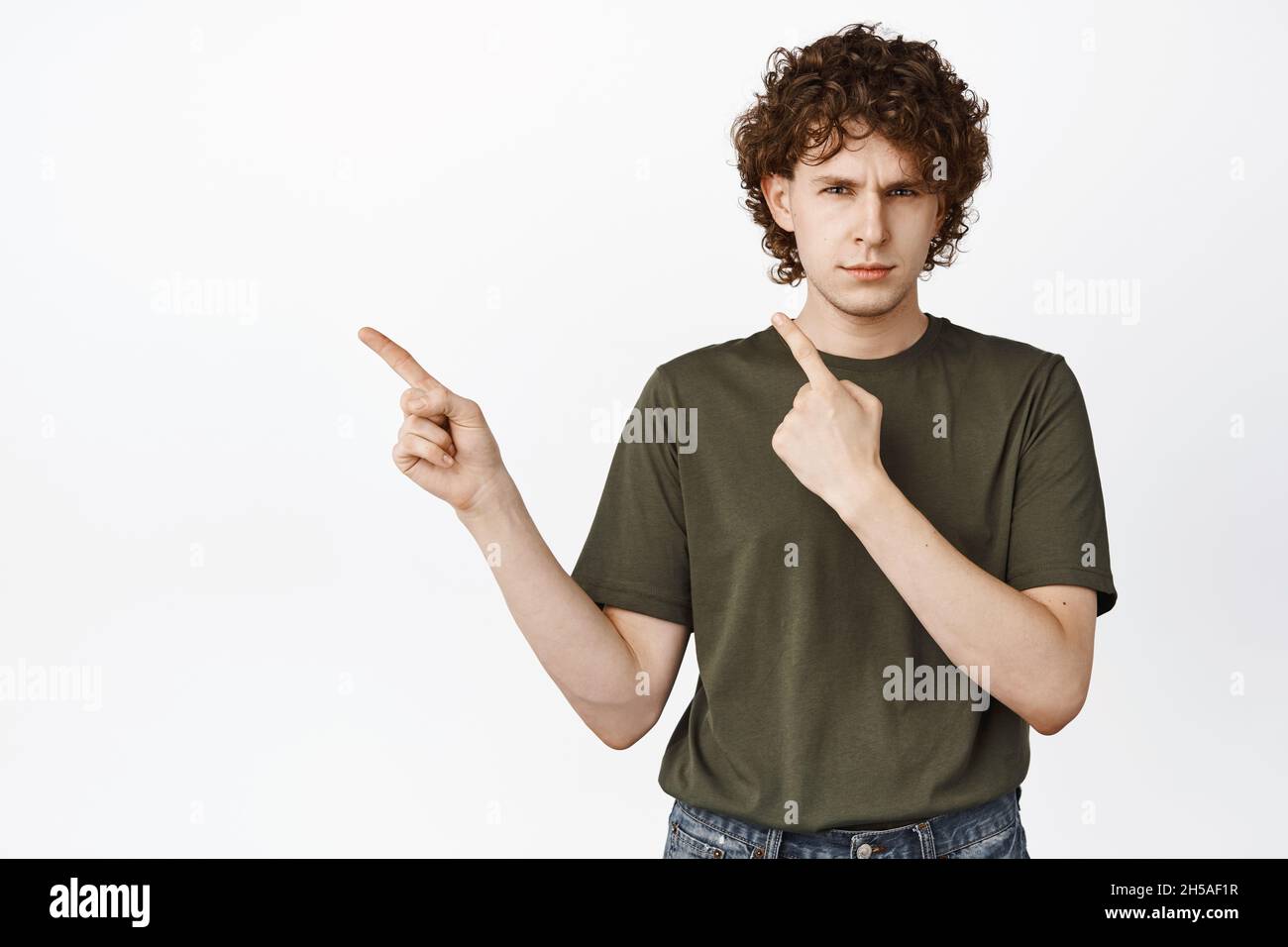 Suspicious teen guy pointing fingers at upper left corner, squinting ...