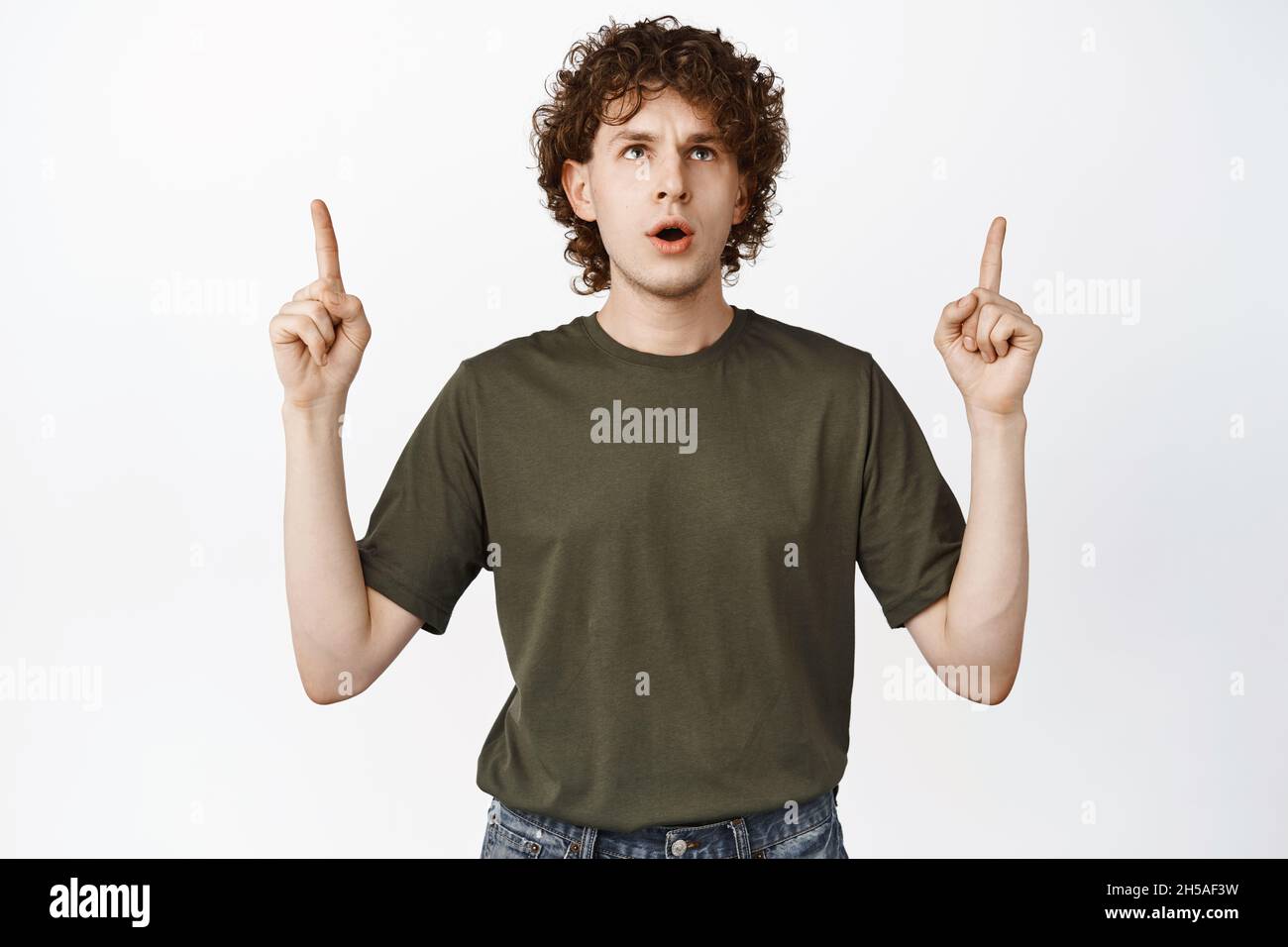 Shocked young man looking and pointing fingers up, staring at ...