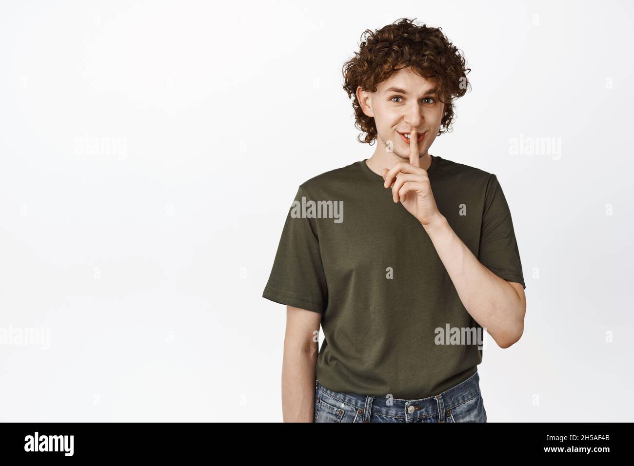 Cute smiling curly-haired man making shhh gesture, shush taboo sign on ...