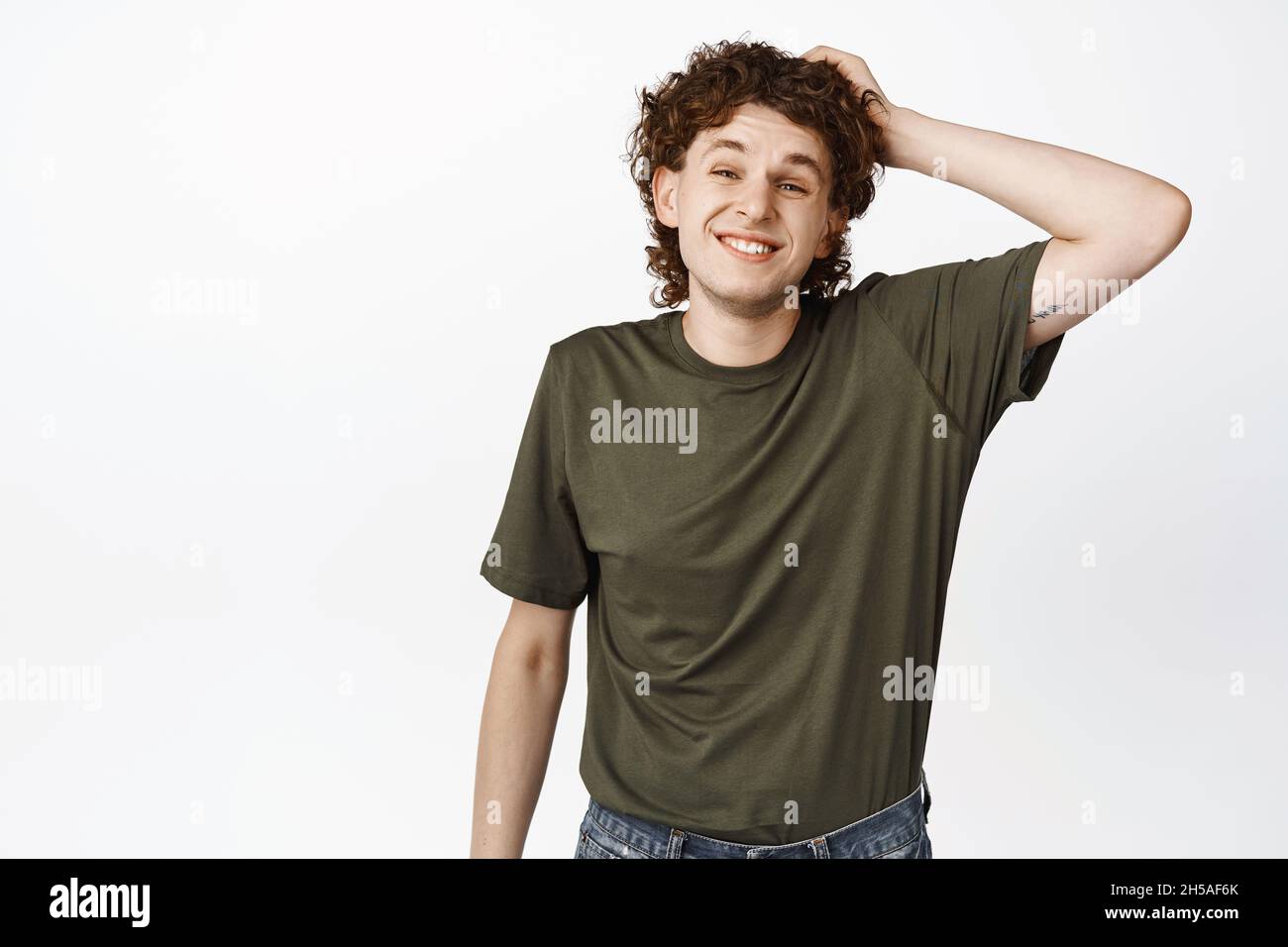 Cute smiling young man with curly hairstyle, scratching head and ...