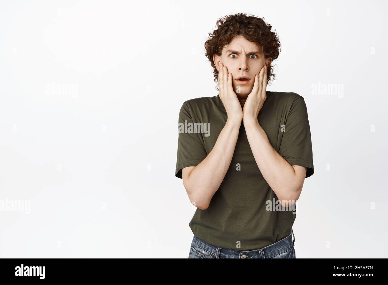 Shocked and concerned young funny guy, staring confused at camera ...
