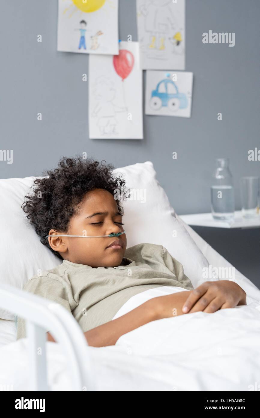 African sick little boy lying in bed at hospital ward with tubes in his ...