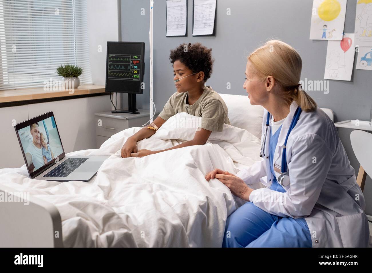 Sick little child sitting in bed together with his doctor and talking ...