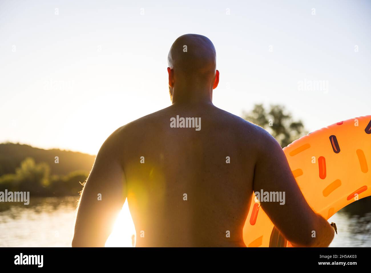 Rearview of a bald man by a lake holding an inflatable donuts Stock ...