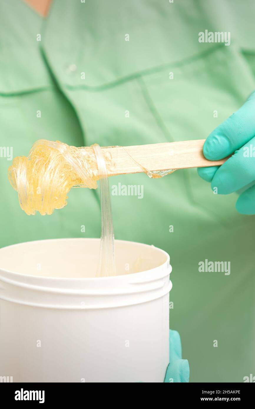 Liquid yellow sugar paste for depilation on a stick flows into the jar ...