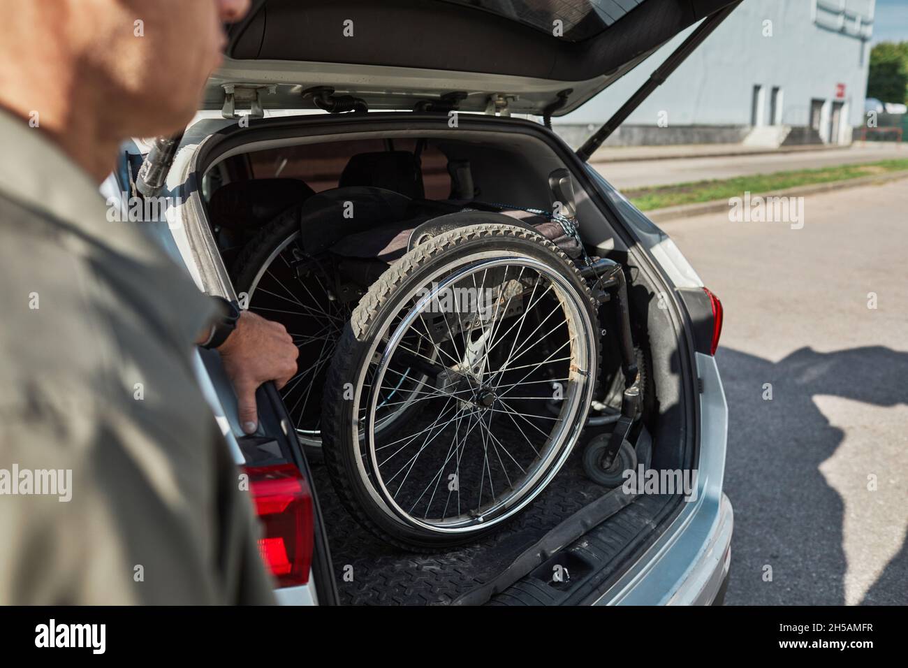 Portrait of unrecognizable man taking wheelchair out of car trunk in ...
