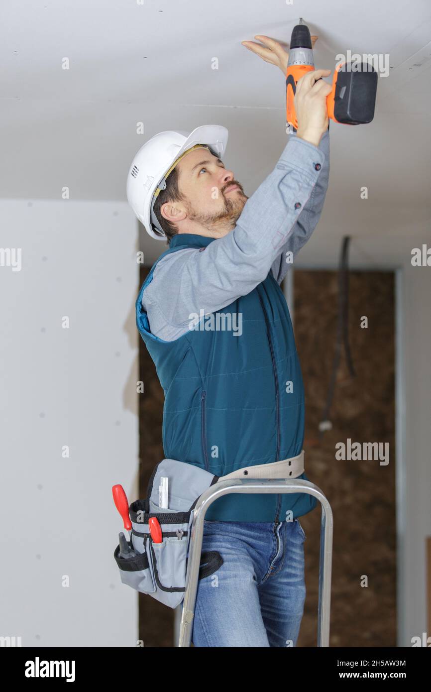 young builder is up a ladder drilling ceiling Stock Photo - Alamy