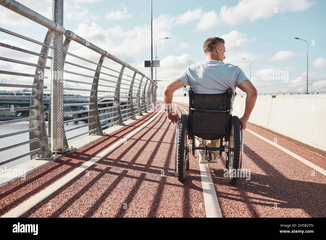 Back view portrait of man in wheelchair in accessible city environment ...