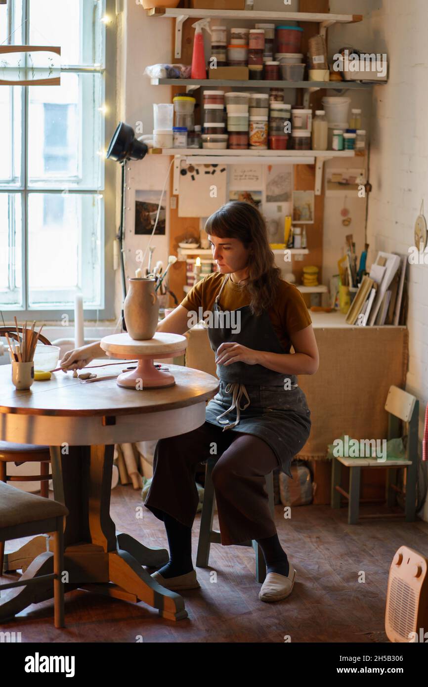 Pottery master at workplace: female sit at table in studio work with ...