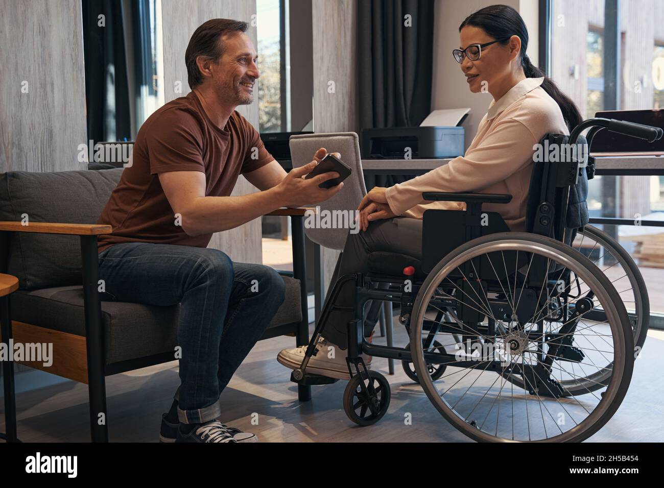 Jolly man with smartphone in office with female with disability Stock ...