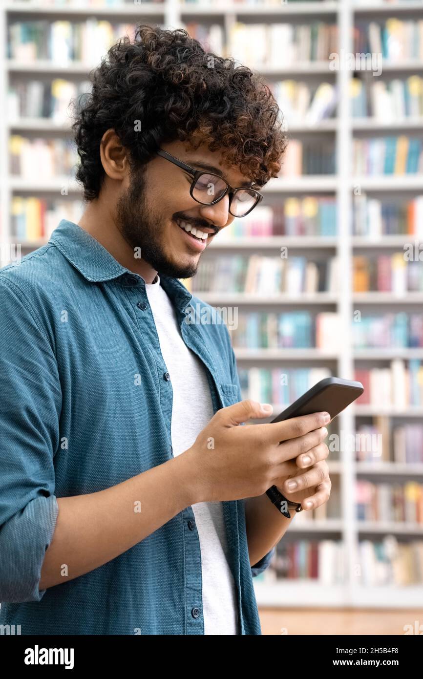 Side view on smart young Indian student using mobile phone in library ...