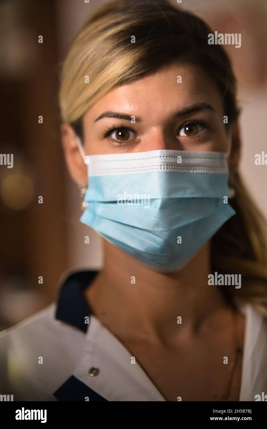 Vertical portrait of a young nurse in a mask looking straight into the ...