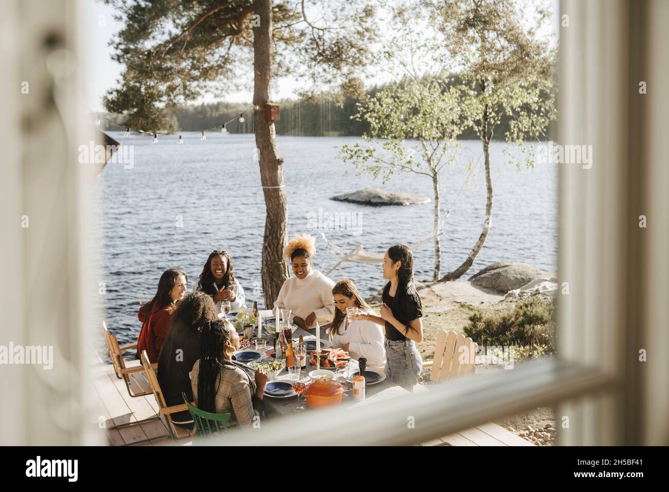 Happy female friends enjoying dinner party seen through window Stock ...