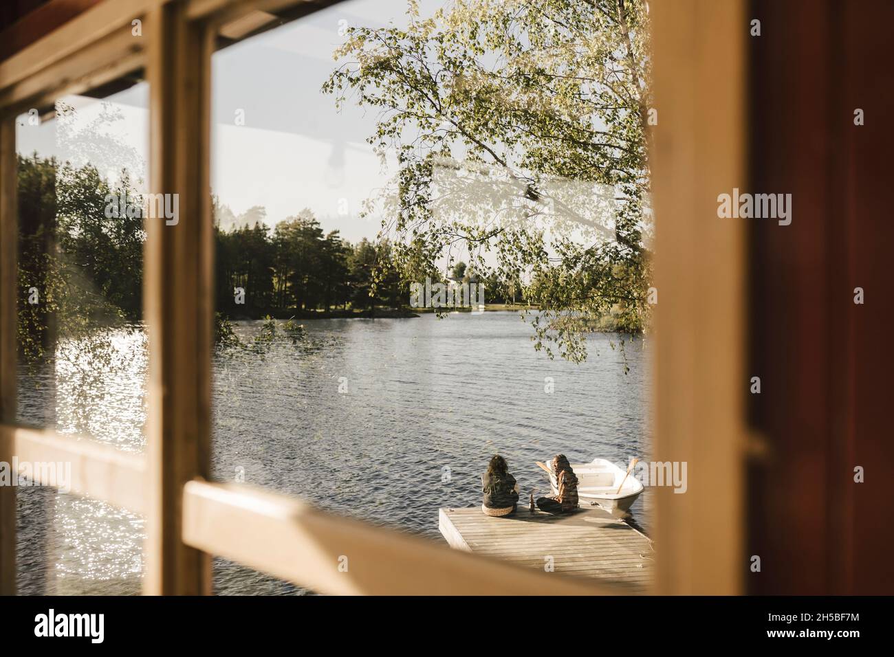 Young female friends sitting on jetty seen through window Stock Photo ...