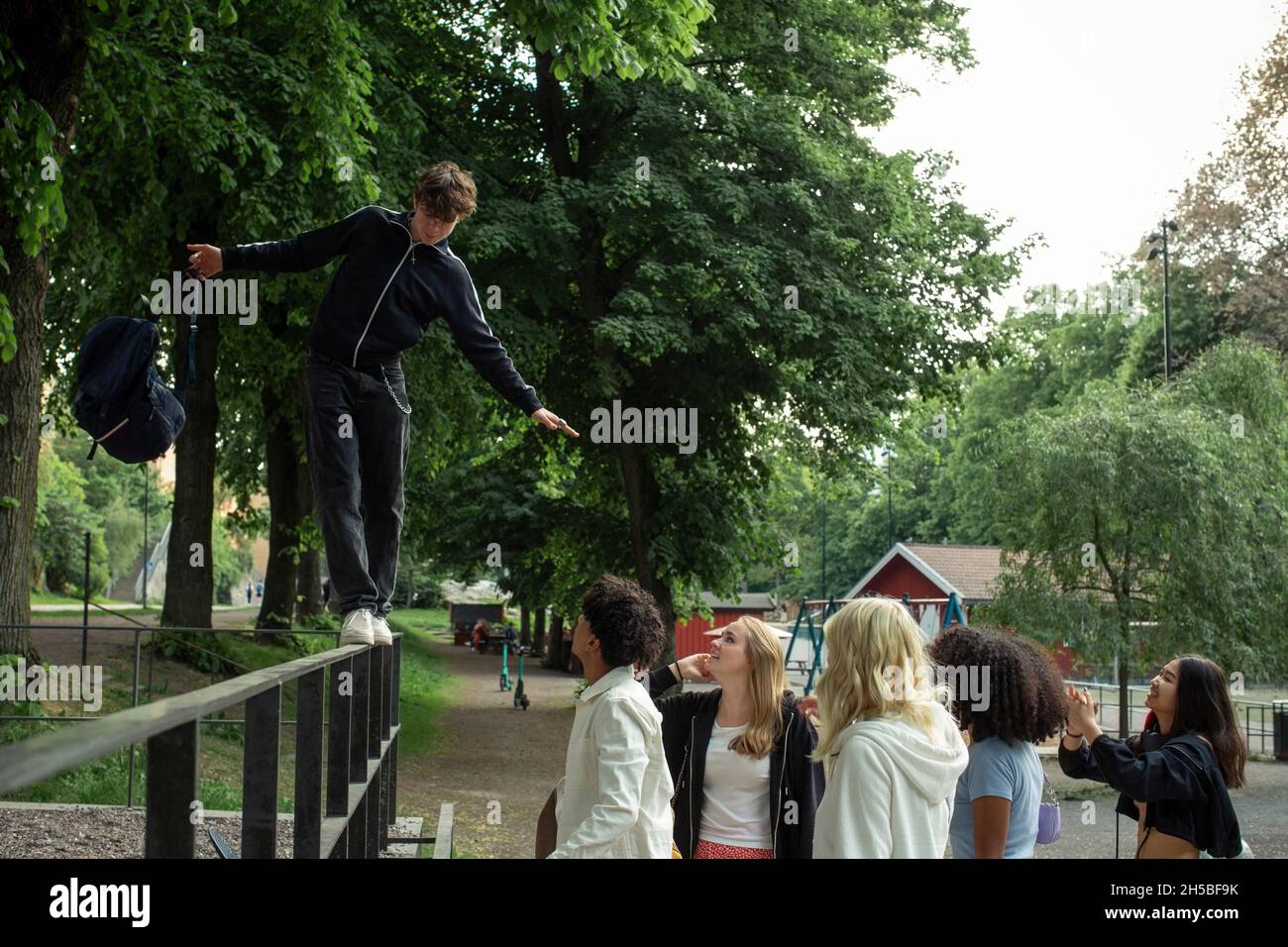 Teenage boy walking on railing while male and female friends looking at ...