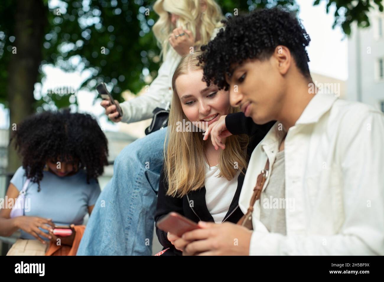 Female and male friends using mobile phones in park Stock Photo - Alamy