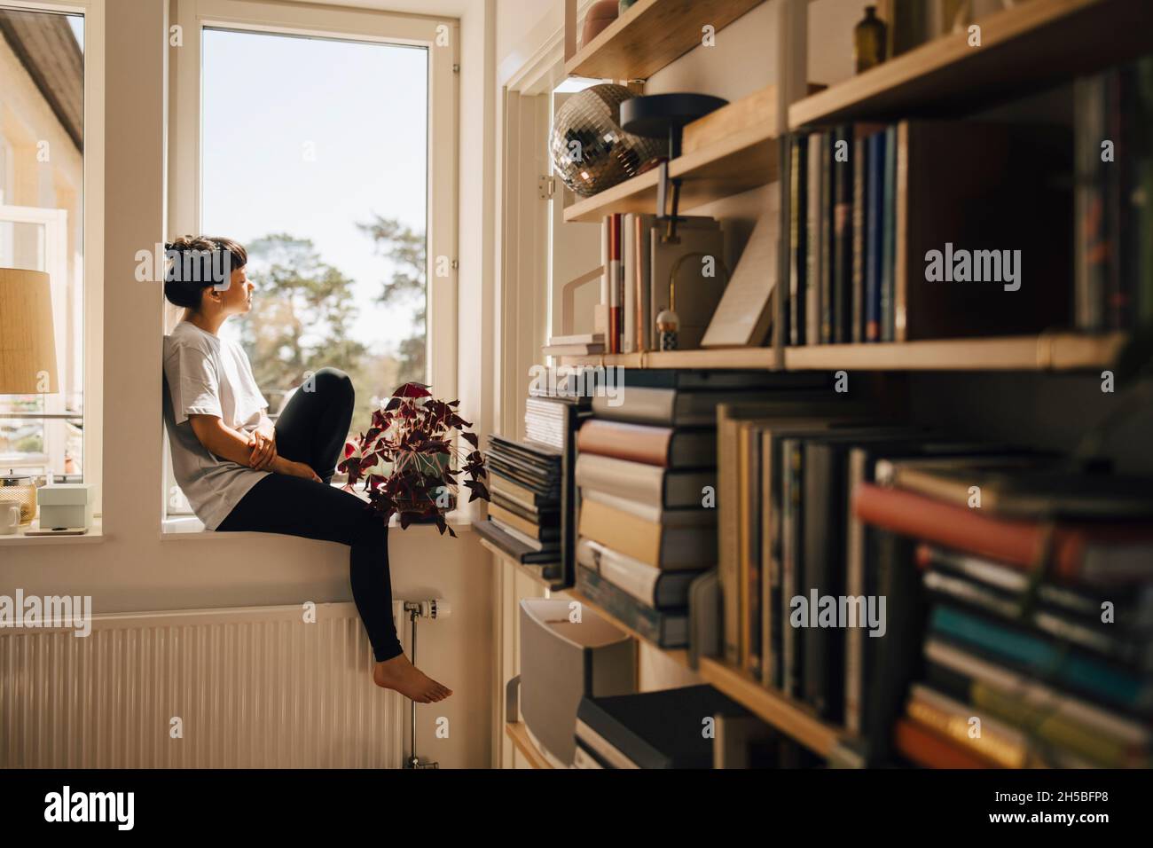 Woman sitting on window seat in sunlight at home Stock Photo - Alamy