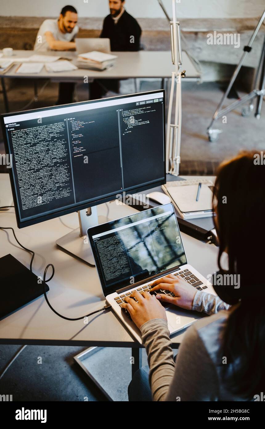 Female programmer coding on laptop at table in creative office Stock ...