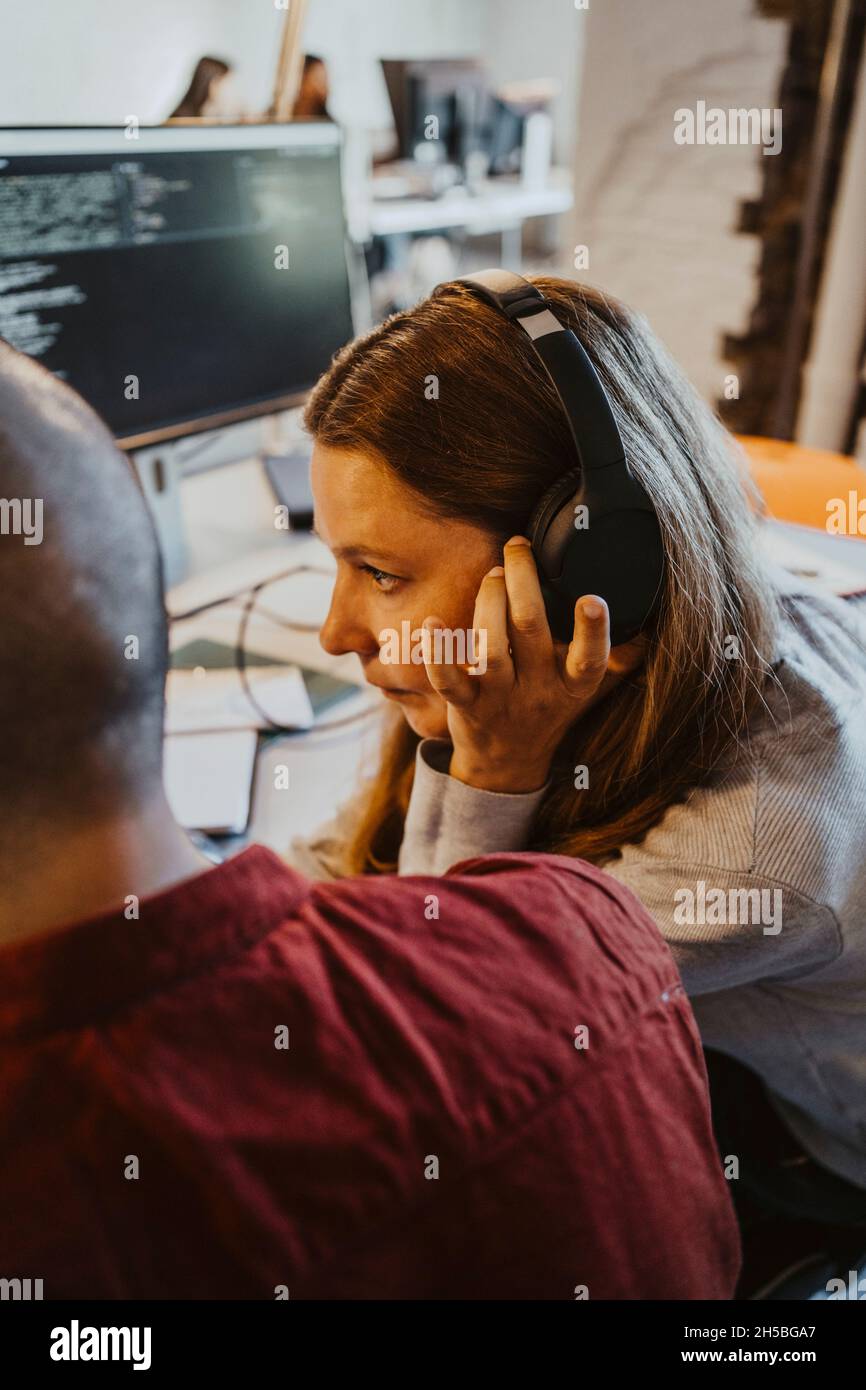 Female programmer listening through headphone while doing coding at ...