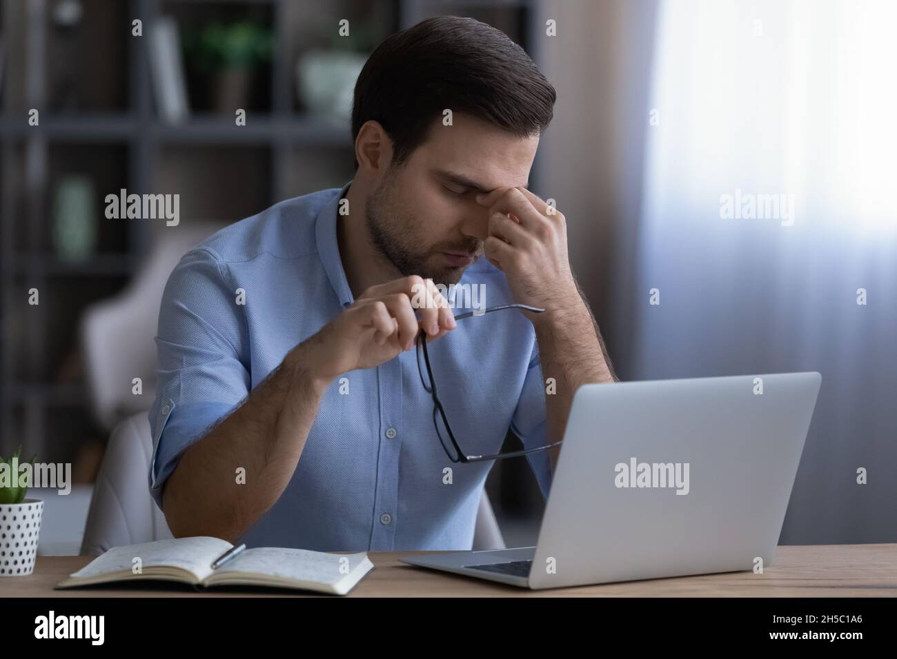 Stressed young male employee taking off eyeglasses Stock Photo - Alamy