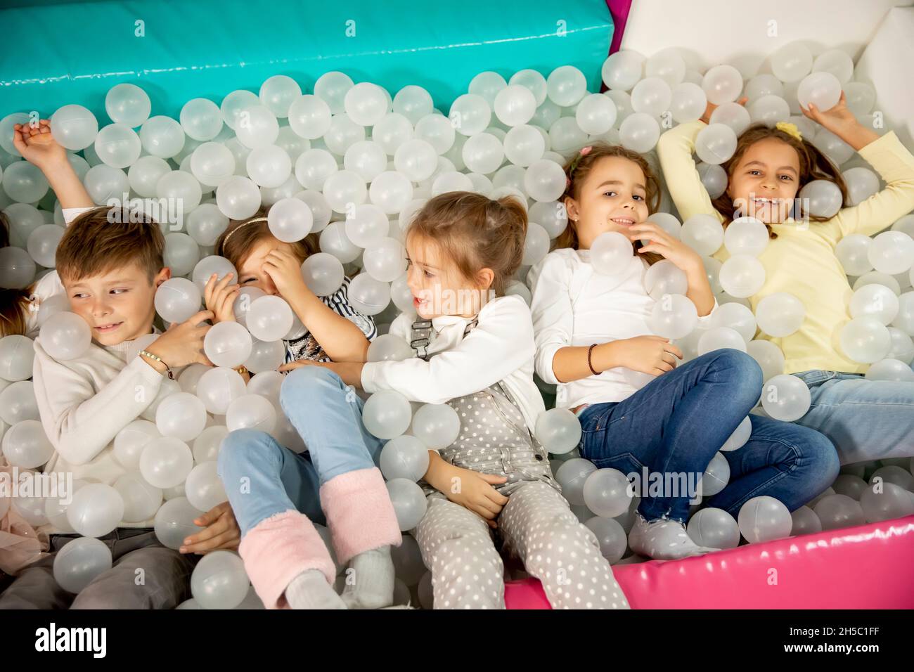 Group of happy little kids in ball pit smiling happily at camera while ...