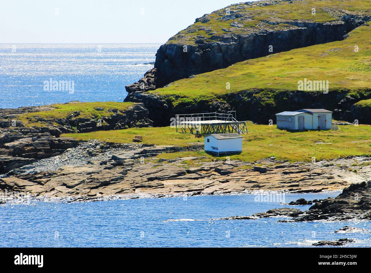 A fishing stage and fishing sheds on a grassy hill, next to the ...