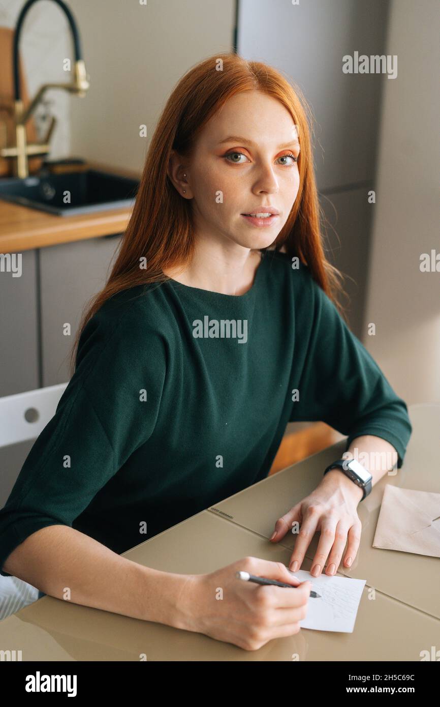 Vertical shot of young woman writing handwritten letter sitting at ...