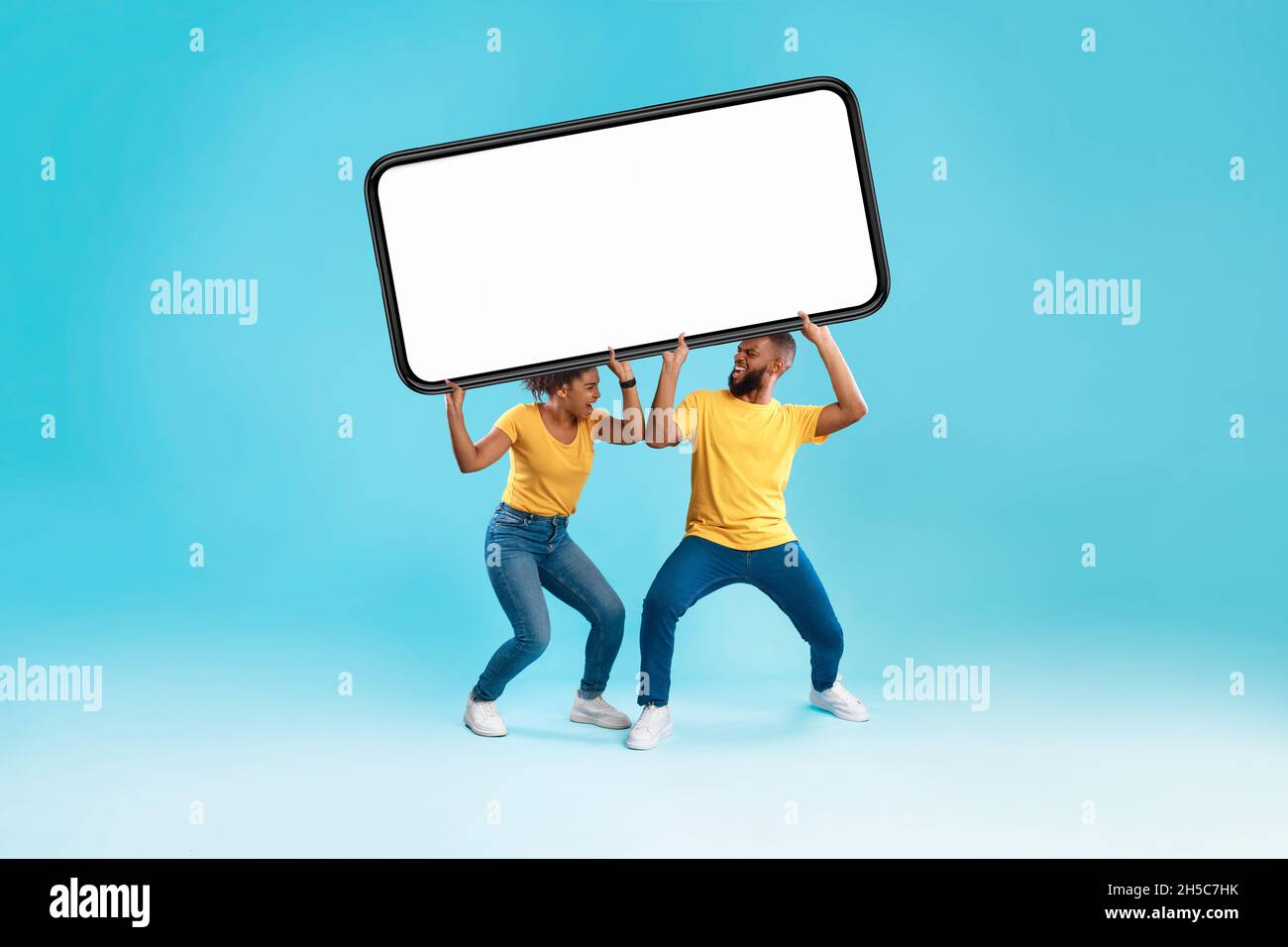 Millennial black couple holding huge heavy cellphone with mockup on ...