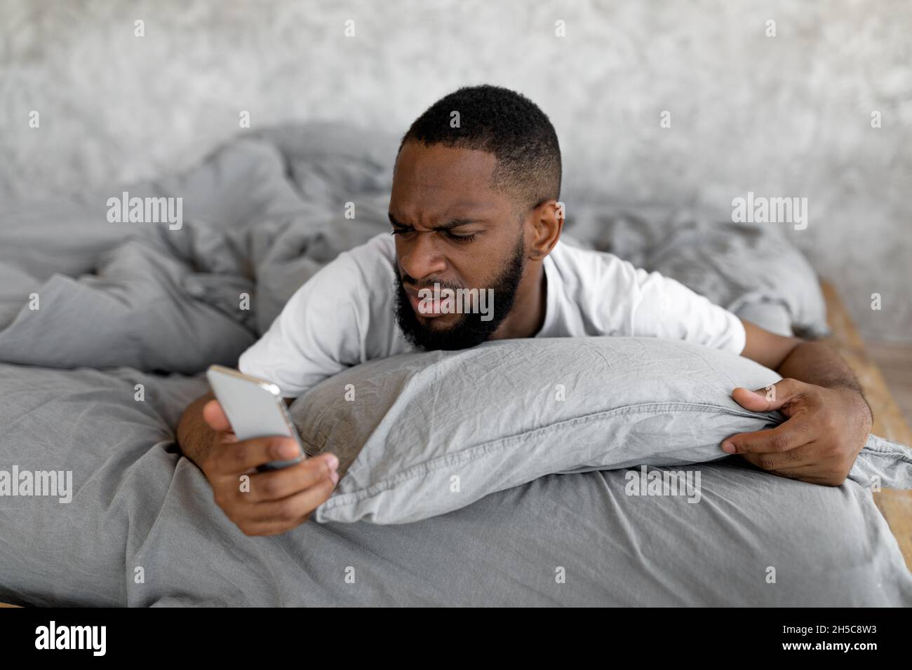 Confused black man looking at phone in bed Stock Photo - Alamy Confused black man looking at phone in bed Stock Photo - Alamy