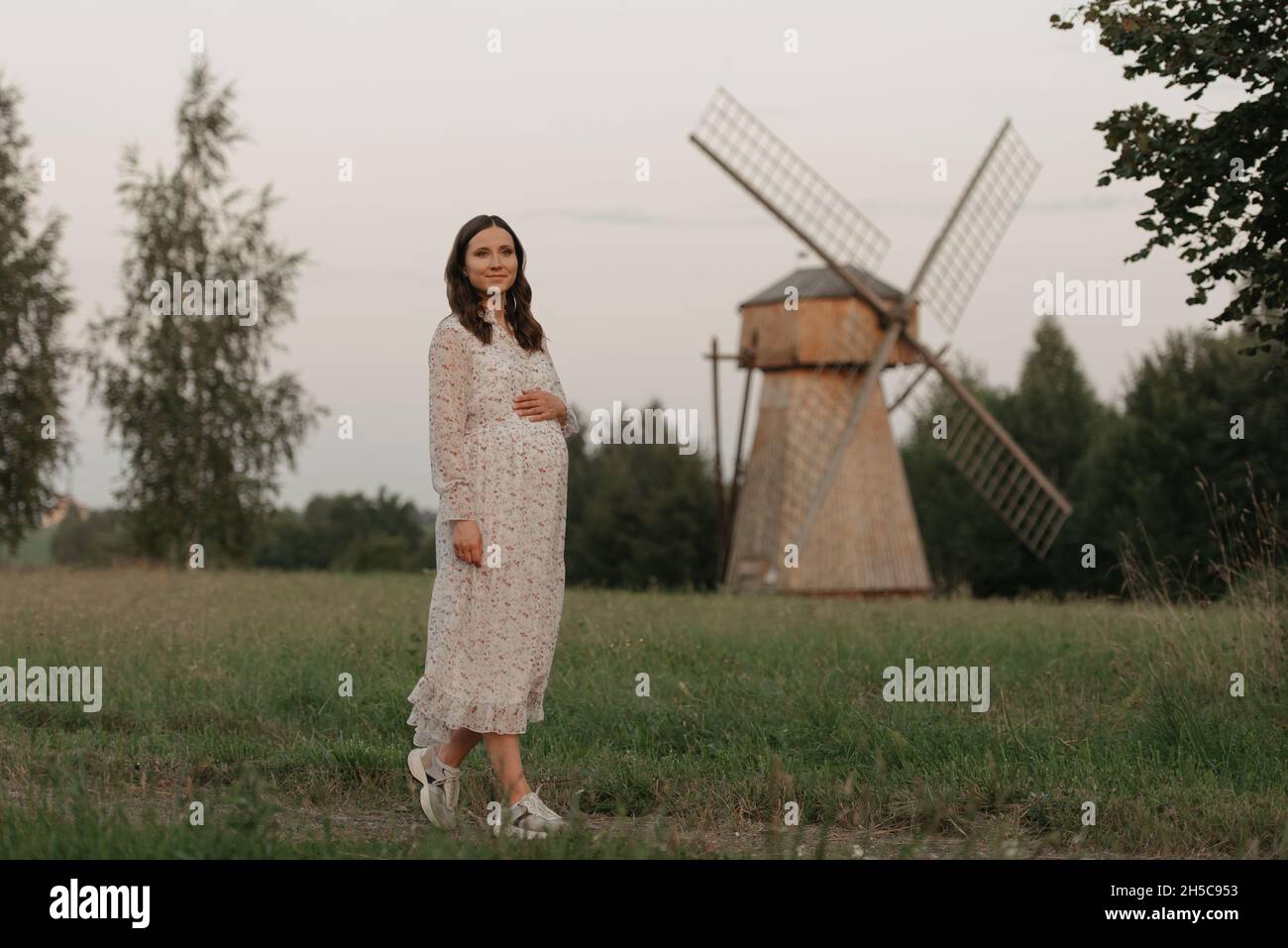 A pregnant woman in the windmill background is holding her belly with ...