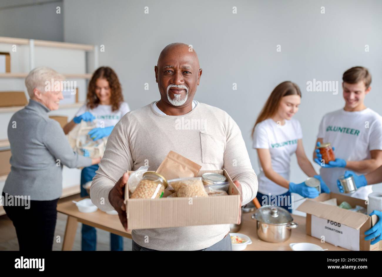 Charity center. Happy black senior man holding box with donations food ...