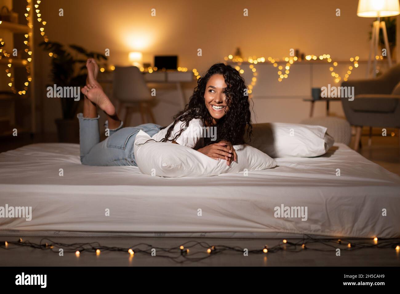 Cheerful Woman Lying On Stomach In Bed Relaxing In Bedroom Stock Photo ...