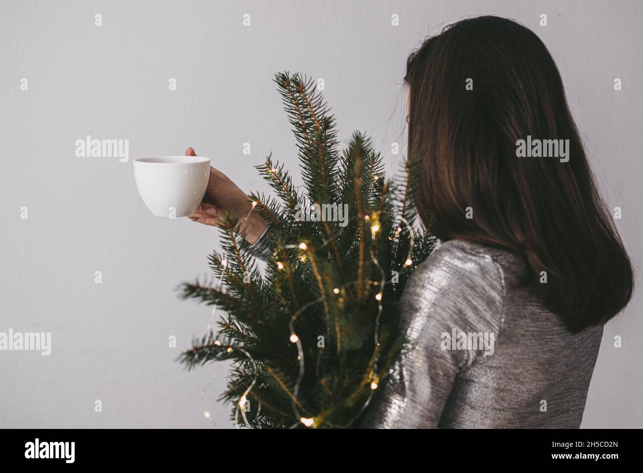 Female hiding his face behind a bouquet spruce branches, holding a cup ...