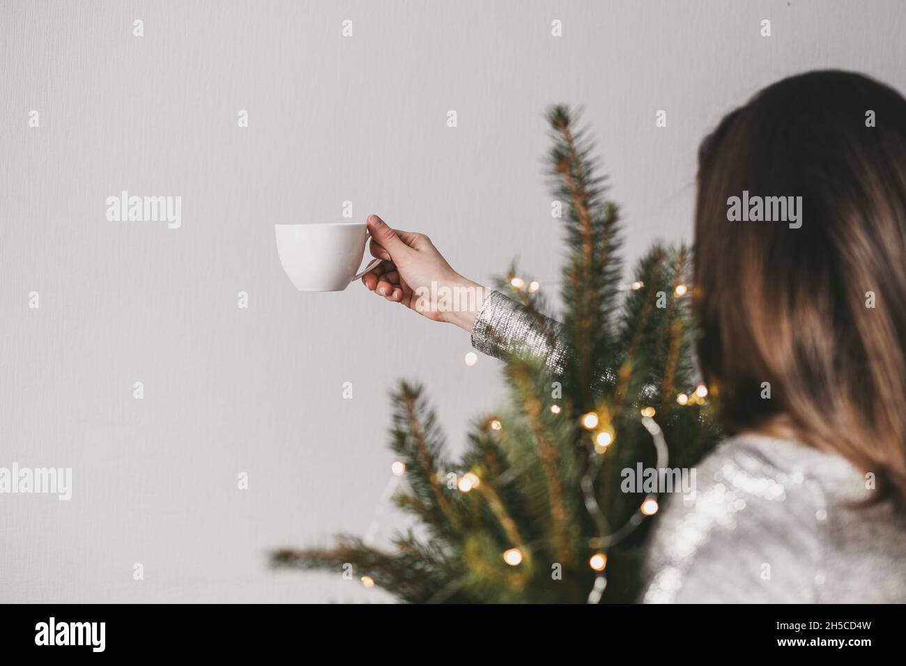 Female hiding his face behind a bouquet spruce branches, holding a cup ...