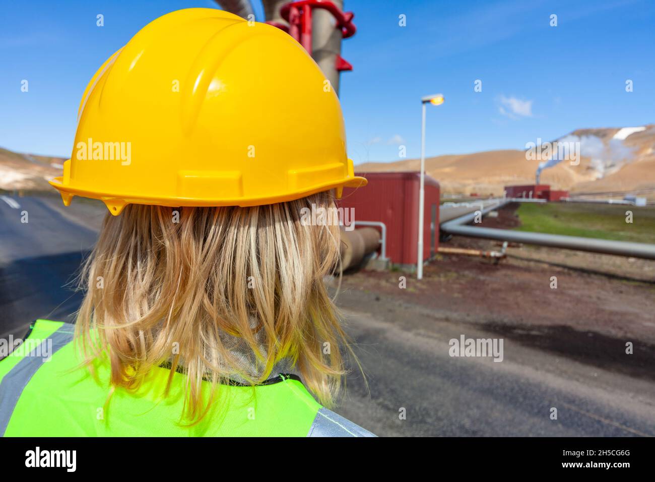 Rear view of a female woman worker wearing a hardhat working at a green ...