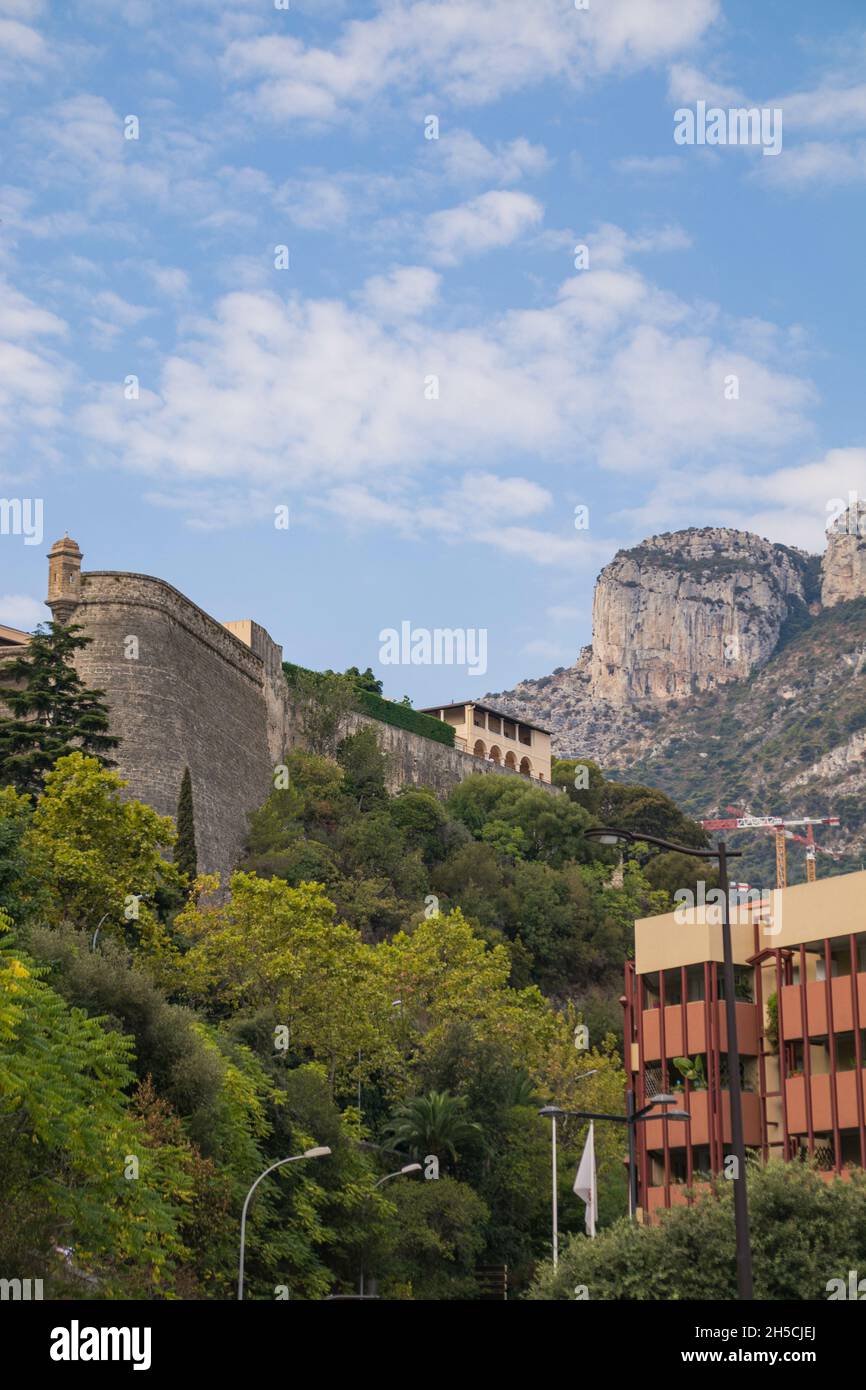 Vertical shot of buildings, rocks and trees under a blue sky with tiny ...