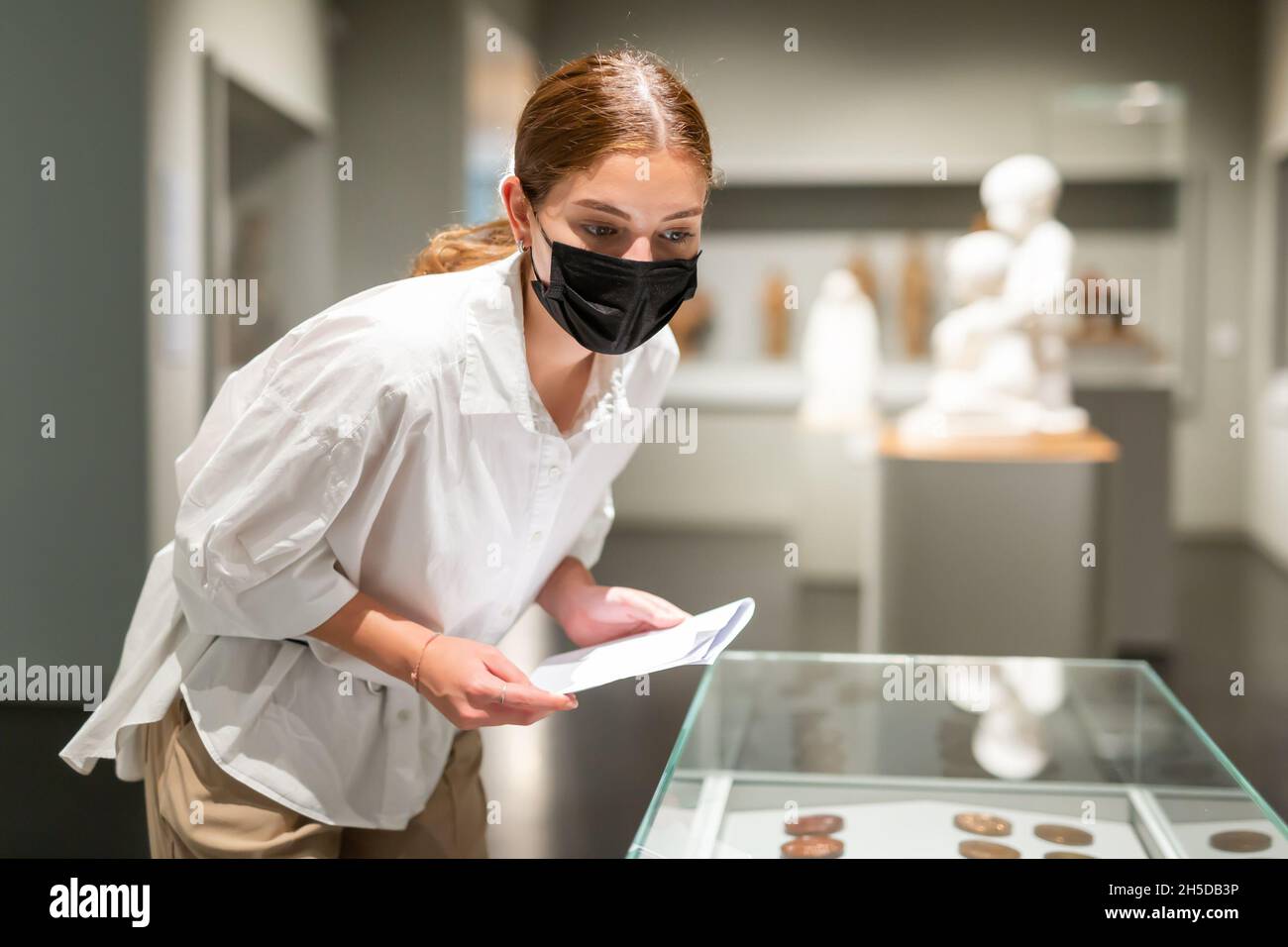 Female in mask looking at the exposition of ancient coins Stock Photo ...