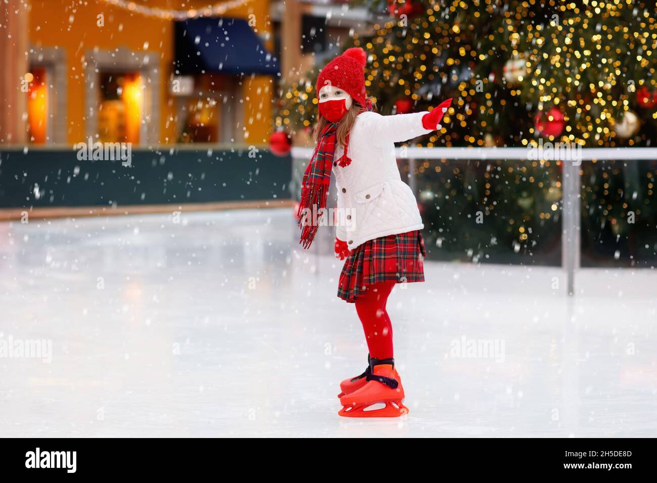 Kid in face mask ice skating in winter park rink. Safe Christmas fun in ...